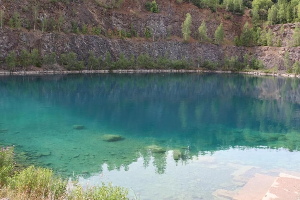 Um lago límpido rodeado por terreno rochoso e vegetação escassa.