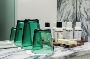 Uma bancada de mármore com garrafas de vidro verde e frascos de higiene pessoal brancos.