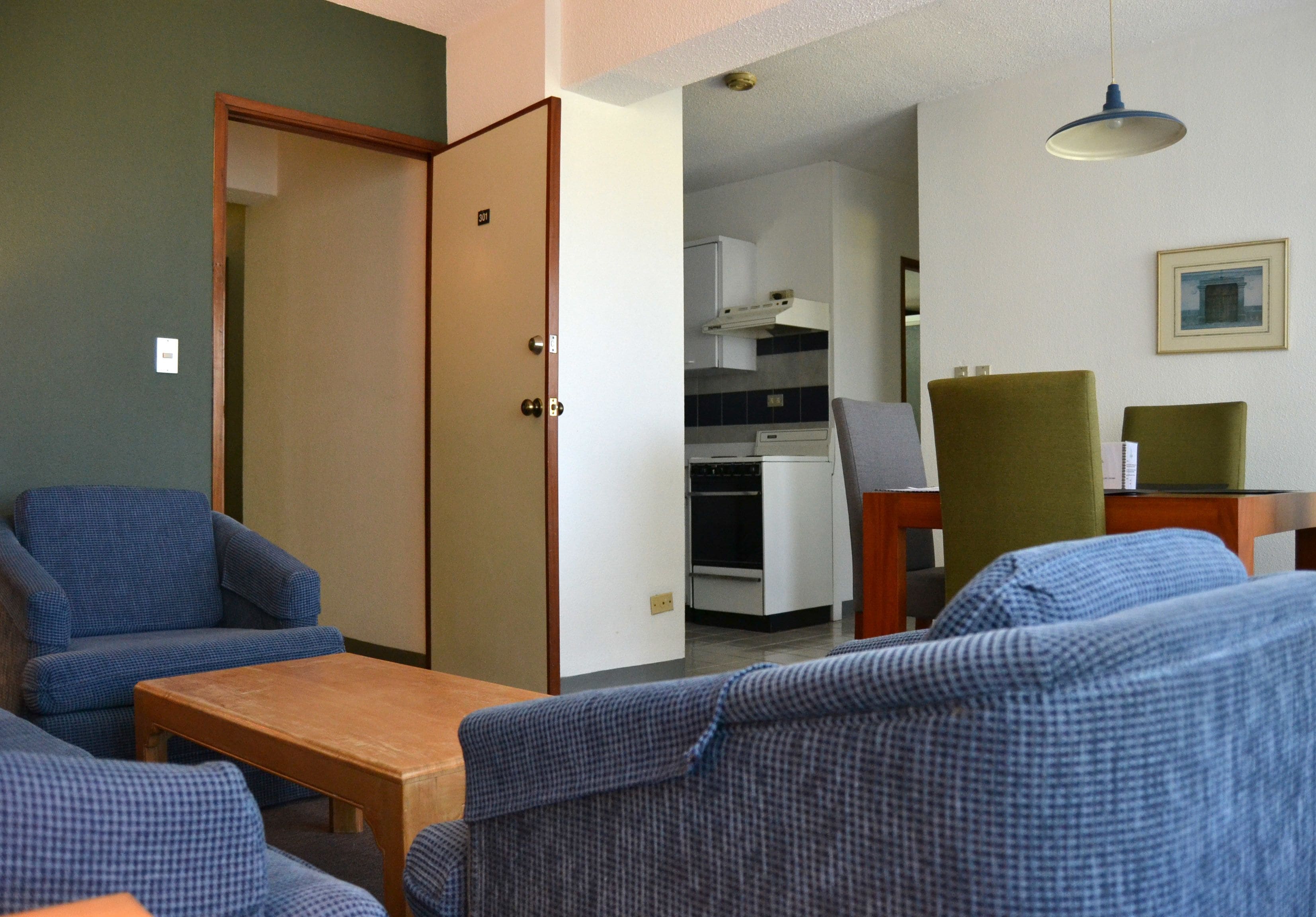 Um espaço de estar compacto com cozinha compacta, área de refeições com mesa e cadeiras, e uma área de estar separada com sofá e poltronas.