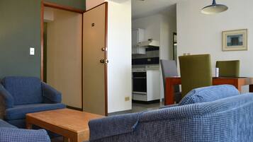 Um espaço de estar compacto com cozinha compacta, área de refeições com mesa e cadeiras, e uma área de estar separada com sofá e poltronas.