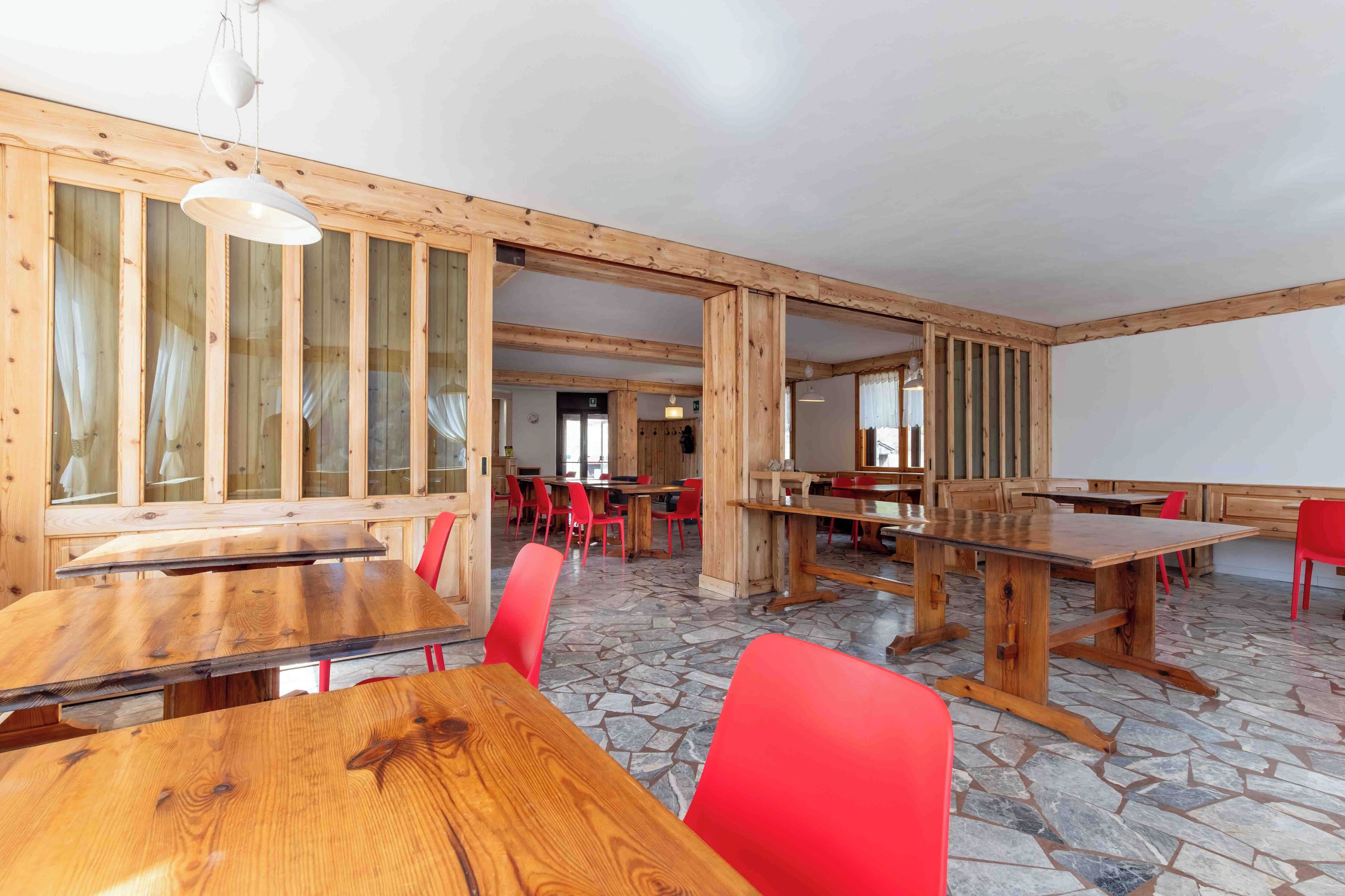Uma sala de jantar com mesas de madeira e cadeiras vermelhas, piso de pedra e vigas de madeira no teto.