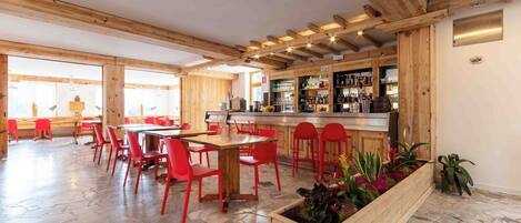 Um restaurante com vigas de madeira, cadeiras vermelhas, um espaço de bar e um chão de pedra.