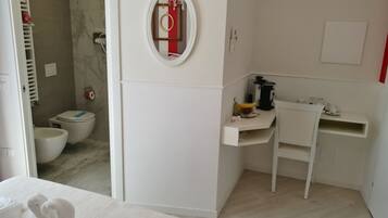 Quarto de hotel com cama, uma secretária pequena com cafeteira, sanita e área de duche.