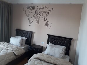 Quarto de hotel com duas camas, cada uma com cabeceira e almofadas, e um mapa-múndi na parede.