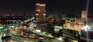 Paisagem urbana noturna com edifícios iluminados, uma autoestrada e outdoors.