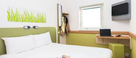 Quarto de hotel com uma cama, uma secretária com um laptop, uma televisão e uma janela.