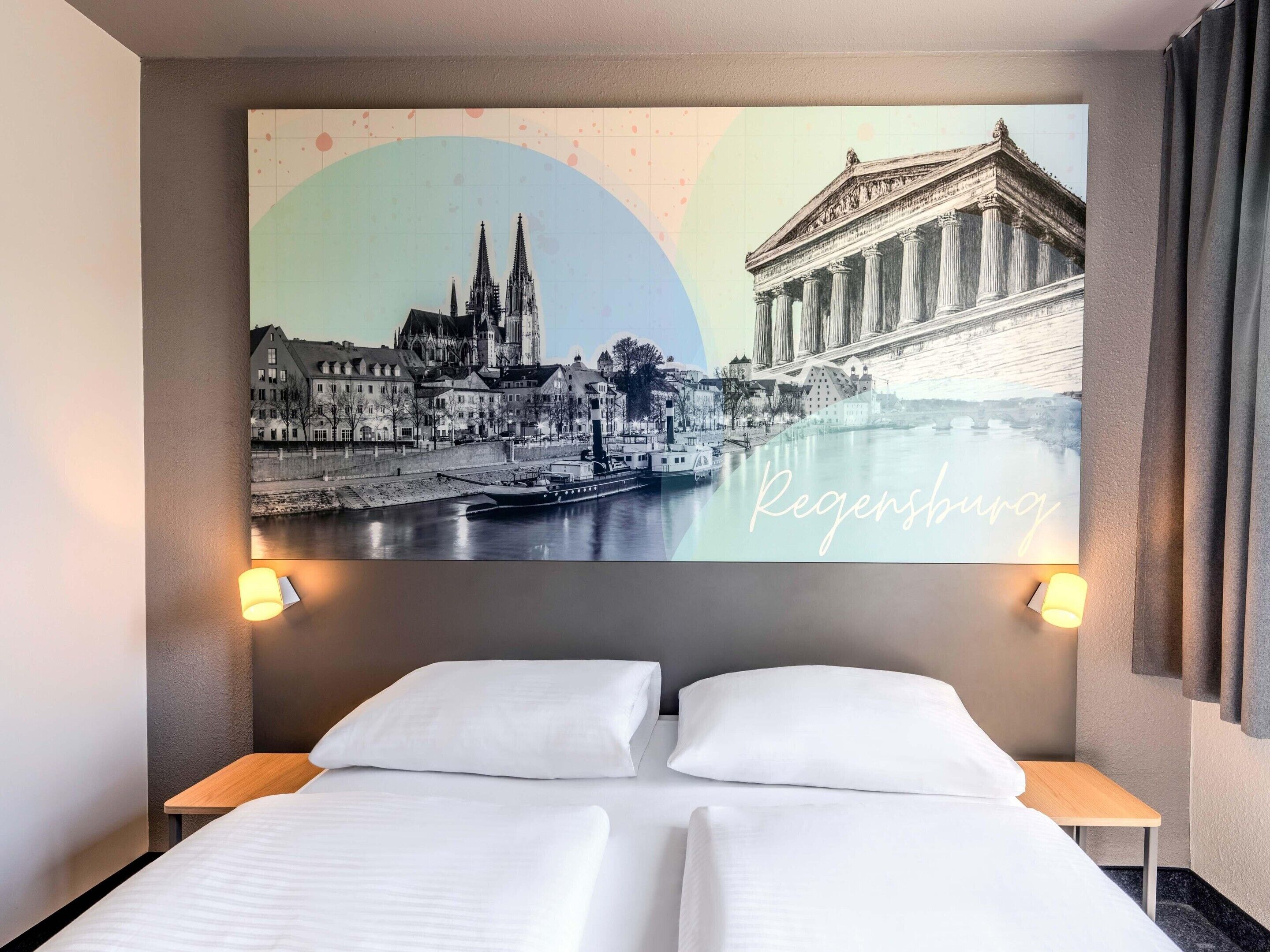 Quarto de hotel com uma cama, duas mesas de cabeceira e uma grande obra de arte com vista para a cidade na parede.