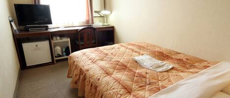 Quarto de hotel com cama, escrivaninha, computador, pequeno frigorífico e televisão.