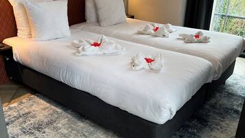 Quarto de hotel com uma cama grande, duas almofadas, cabeceira, mesa de cabeceira, tapete e uma janela com cortinas.