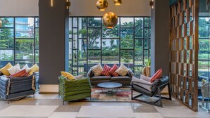 Interior moderno com um conjunto de sofás, uma poltrona verde e uma mesa redonda. Grandes janelas oferecem vista para áreas verdes.