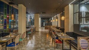 Um restaurante com várias mesas e cadeiras, piso estampado e luminárias pendentes.