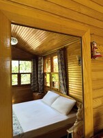 Quarto de cabana de madeira com cama, cortinas e uma figura decorativa.