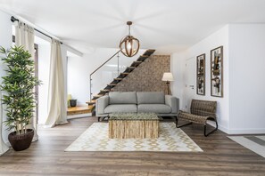 Uma sala de estar moderna com escada, sofá, mesa de centro e uma planta em vaso.