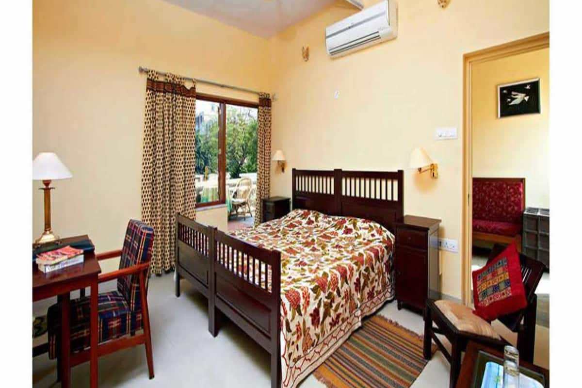 Um quarto com cama, escrivaninha, cadeira, janela com cortinas, ar-condicionado e porta com aviso.