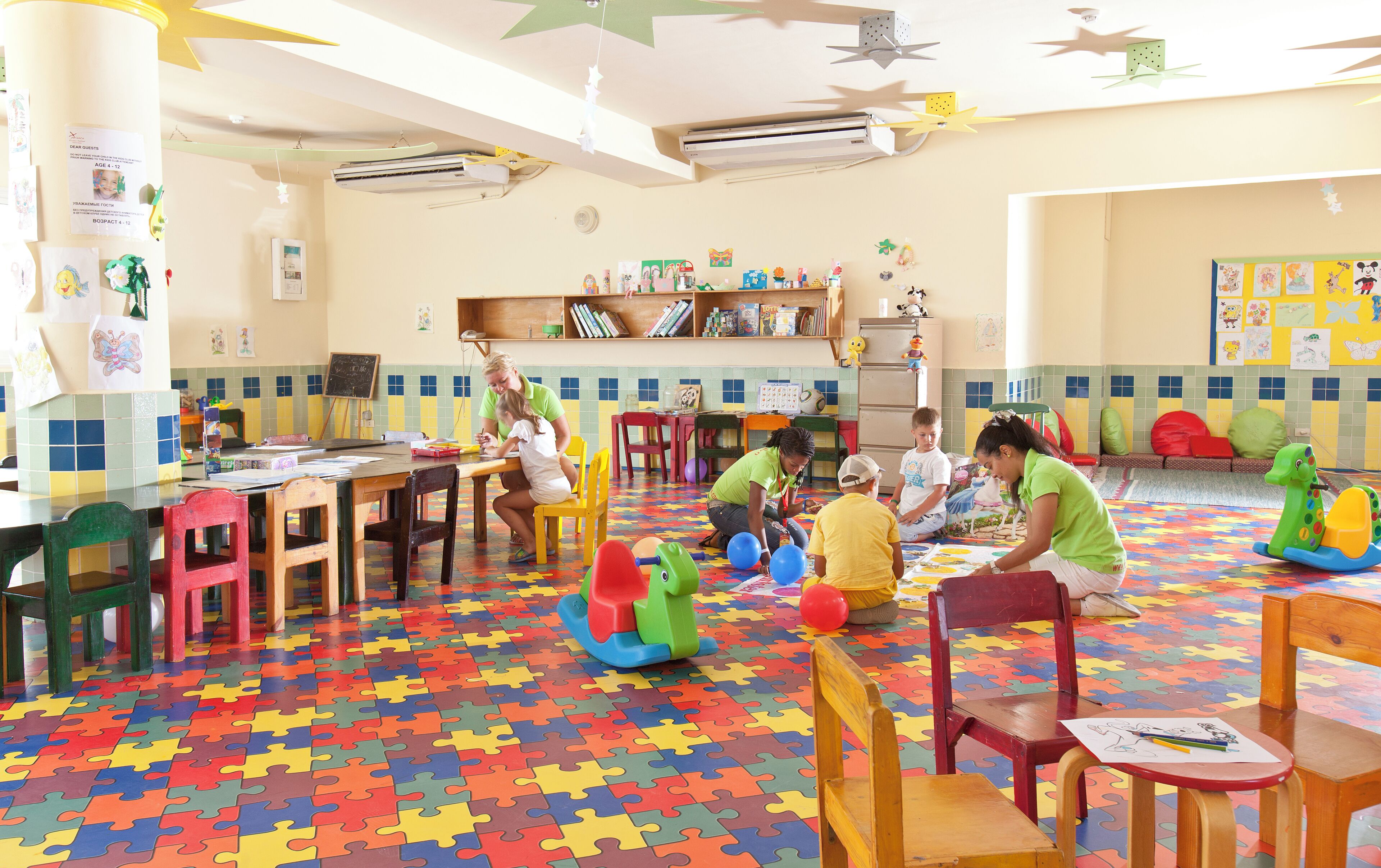 Uma sala de aula vibrante, com crianças participando em atividades, destacando um chão com mosaico de quebra-cabeças e materiais educativos.