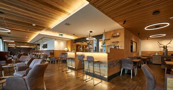 Restaurante moderno com teto de madeira e área de bar, com mesas e um chifre decorativo na parede.