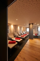 Uma sala de spa com várias cadeiras de massagem, piso de madeira e teto perfurado.