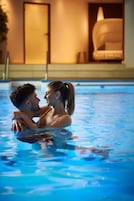 Um casal em uma piscina, com uma cadeira e uma porta ao fundo.