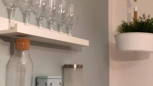 Uma estante com vários copos de vinho, uma garrafa com rolha e uma caixa decorativa com desenho de bule.