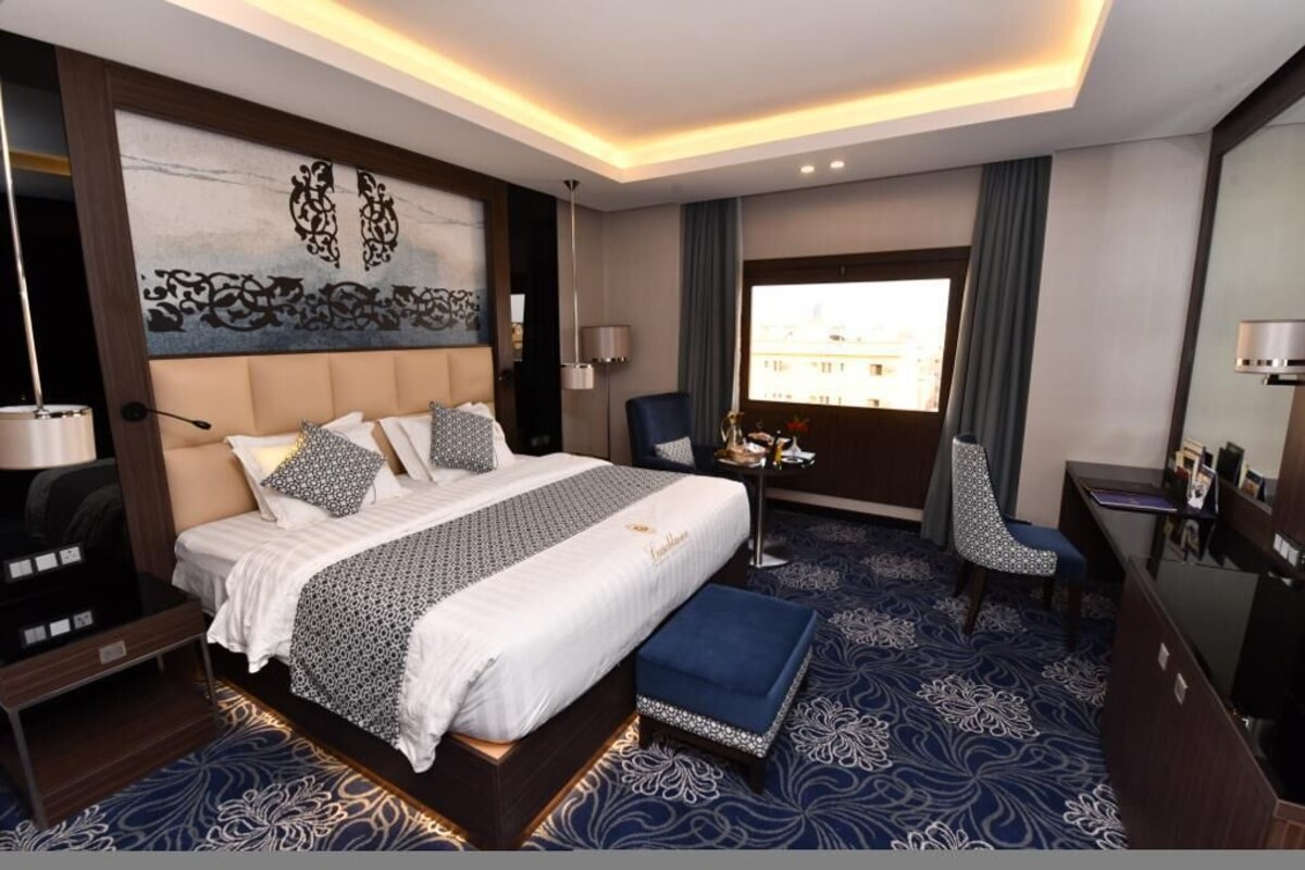 Quarto de hotel com uma cama grande, uma escrivaninha, uma cadeira e uma televisão.