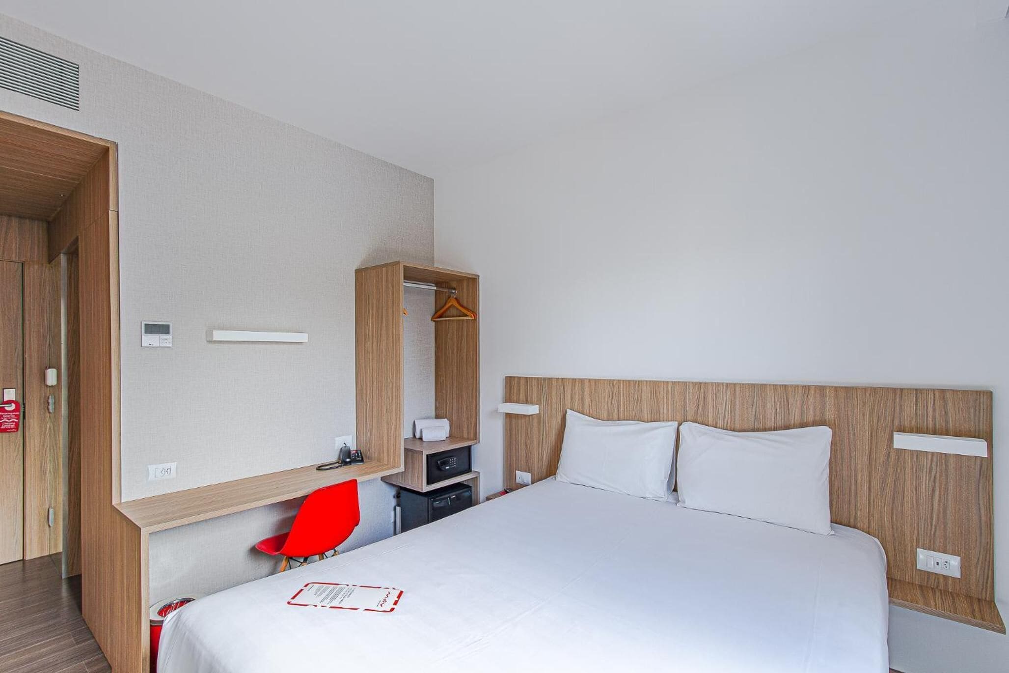 Quarto de hotel com cama, escrivaninha, cadeira, guarda-roupa e espelho.