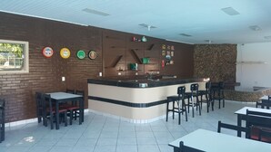 Restaurante com bar central, paredes de tijolo e chão de azulejos.