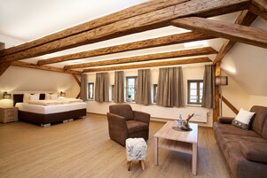 Um quarto espaçoso com uma cama grande, teto de madeira, sofá, mesa pequena e uma cadeira.