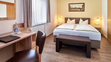 Quarto de hotel com cama, mesas de cabeceira, escrivaninha, cadeira e janela com cortinas.