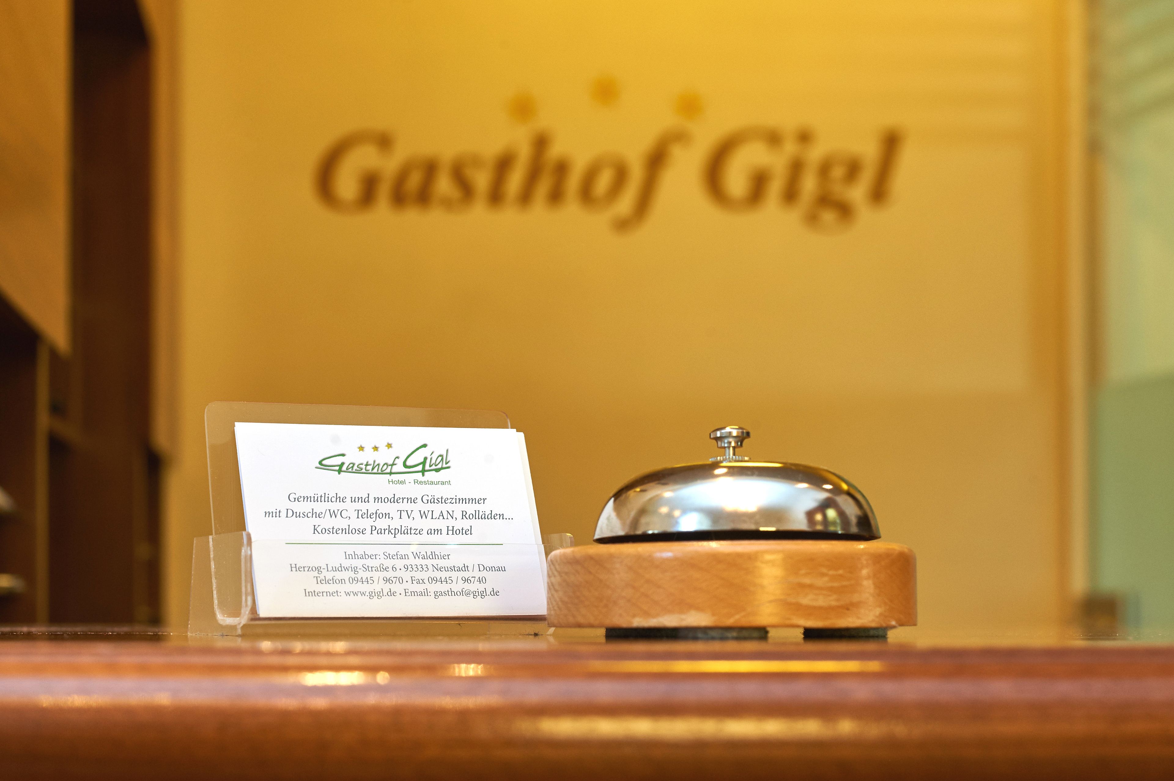 Uma área de recepção de hotel com uma placa indicando 'Gasthof Gigl' e um sino de atendimento.