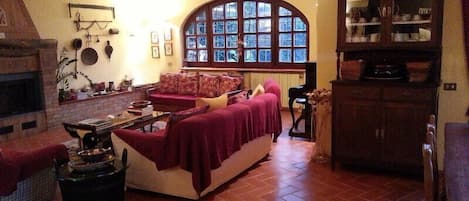 Uma sala de estar acolhedora com lareira, uma grande janela em arco e uma coleção de cerâmica nas prateleiras.