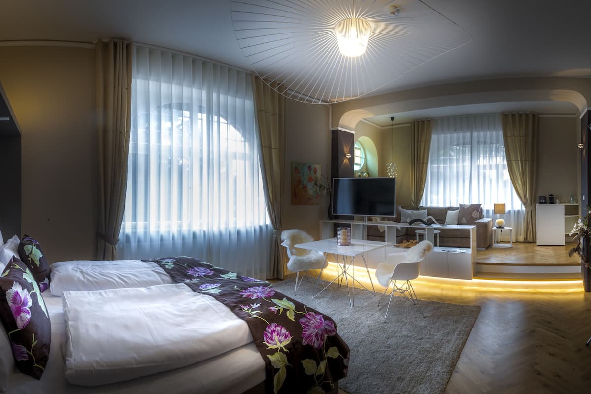 Quarto de hotel moderno com cama, escrivaninha, televisão e área de estar.