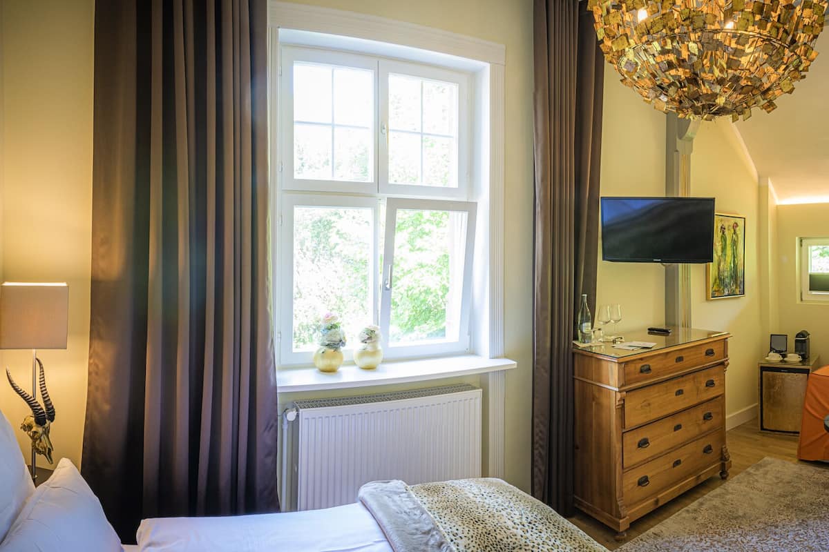 Quarto com uma janela grande, cômoda de madeira, sofá laranja e televisão na parede.