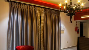 Quarto com cadeira vermelha, lustre e cortinas.