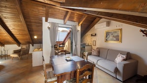 Um loft espaçoso com teto alto, vigas de madeira, área de jantar com mesa e cadeiras, um sofá e um quadro na parede.