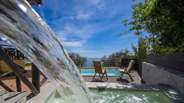Piscina no terraço com cachoeira, duas espreguiçadeiras de madeira e vista para o mar.