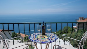 Mesa com uma garrafa e dois copos numa varanda com vista para o mar.
