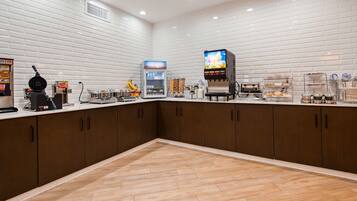 Uma área de café da manhã moderna com estação de autoatendimento, máquina de café e tela de exibição.