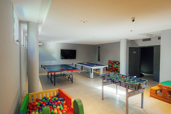 Uma sala de lazer com mesas de pingue-pongue, mesa de futebol de mesa e uma piscina de bolinhas.