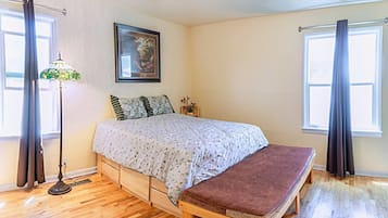 Quarto com cama, um banco, luminária de chão e pintura na parede.