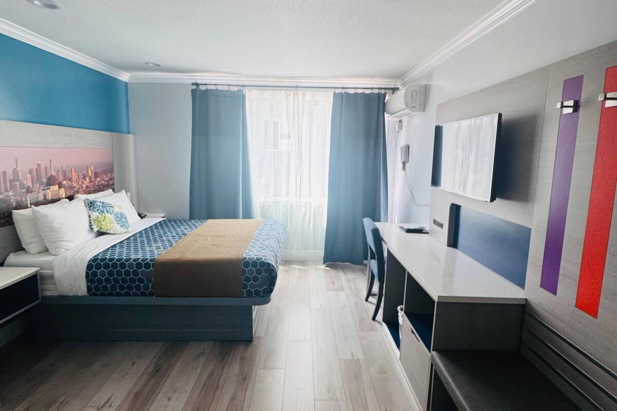 Quarto de hotel moderno com cama, escrivaninha, televisão e um mural com vista para a cidade.