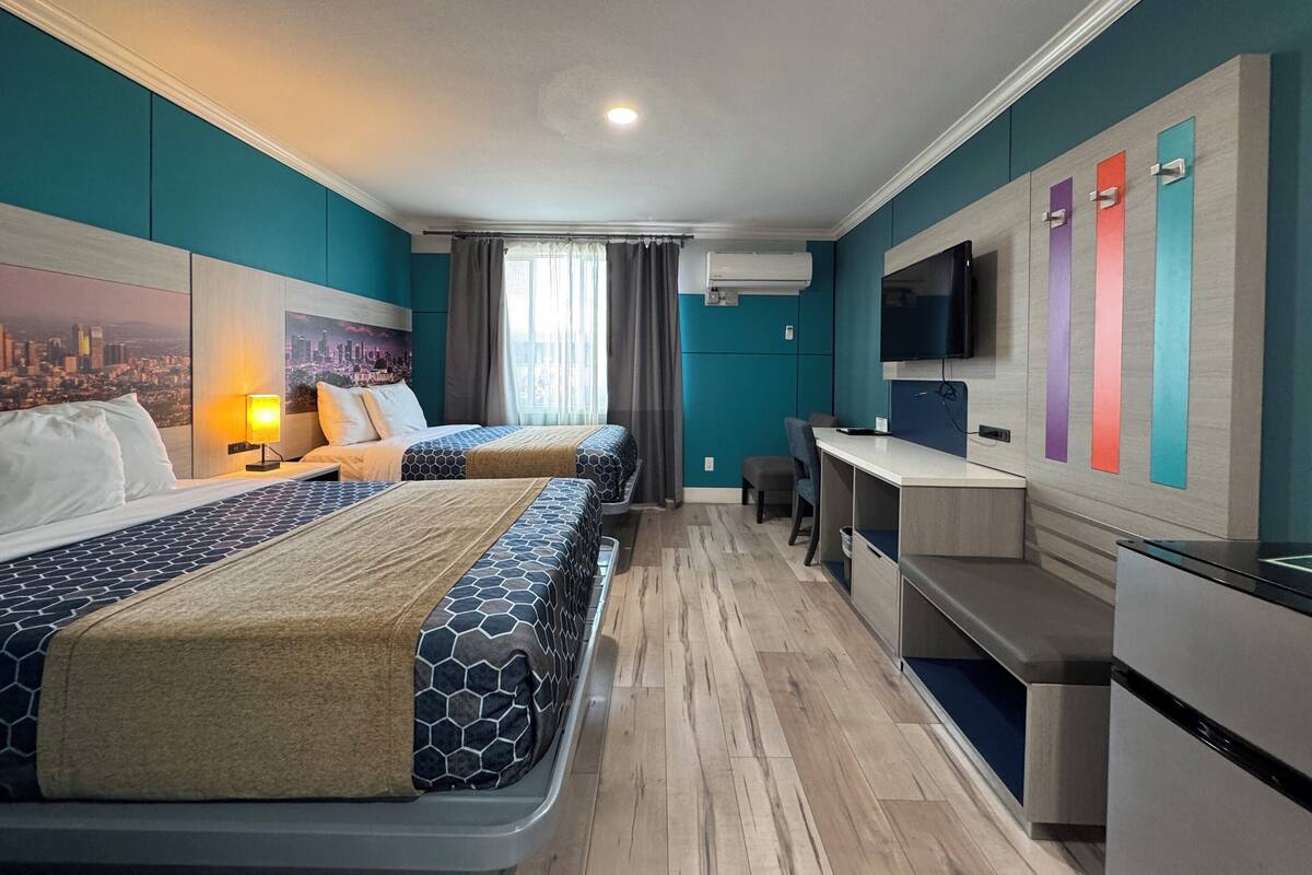 Quarto de hotel com duas camas, uma escrivaninha, uma televisão e um aparelho de ar condicionado.