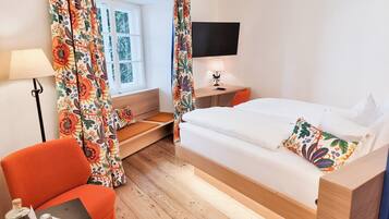 Quarto de hotel com cama, escrivaninha, cadeira, televisão e janela com cortinas.