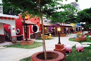 Um pátio com uma fonte central, rodeado por edifícios com designs arquitetônicos únicos e um jardim bem cuidado.