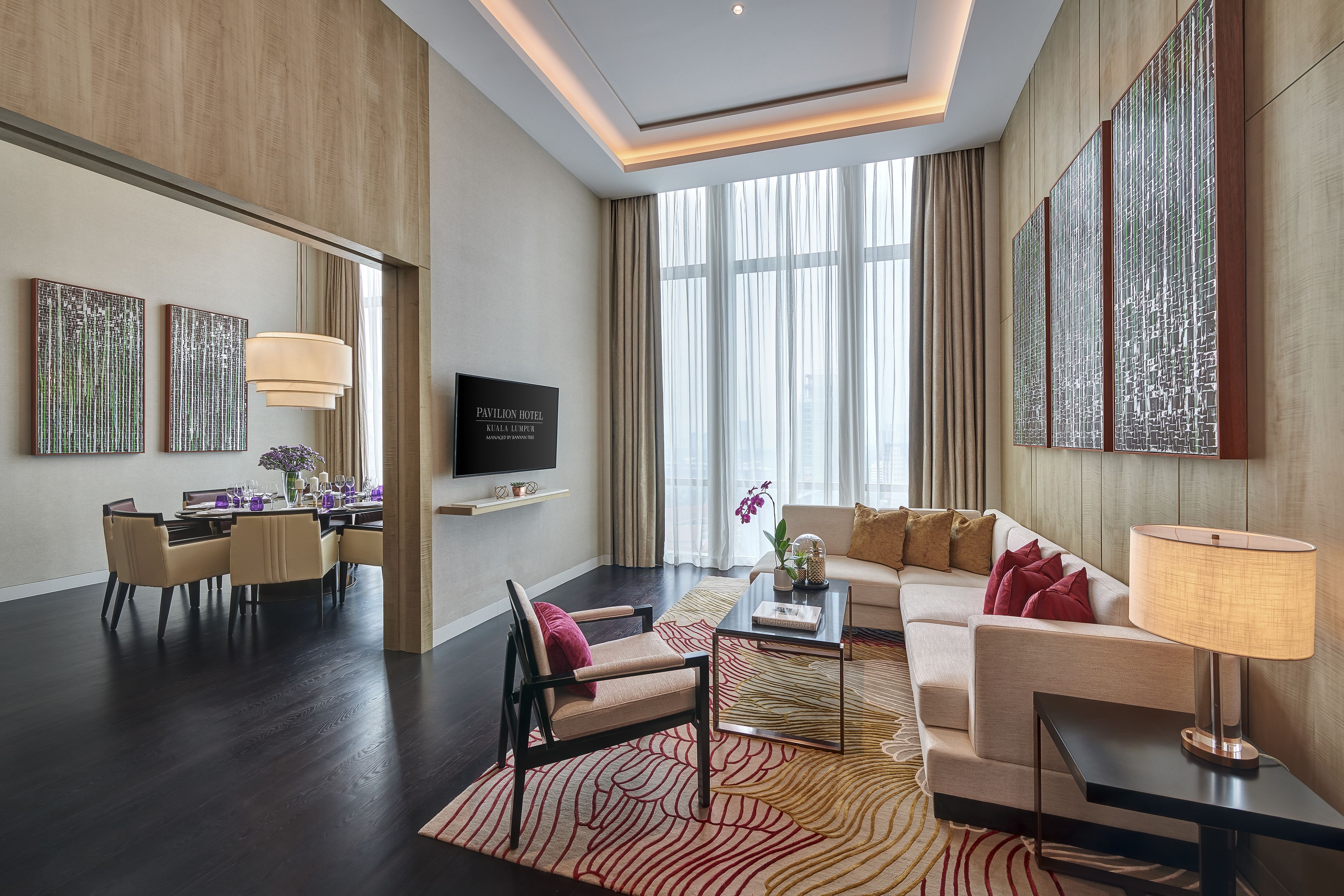 Quarto de hotel moderno com área de refeições, sofá, mesa de centro e televisão.