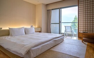 Quarto de hotel com uma cama grande, varanda com cadeira e vista para o exterior.