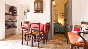 Uma área de jantar acolhedora com uma mesa e cadeiras de madeira, um armário com portas de vidro e vista para um quarto por uma porta aberta.