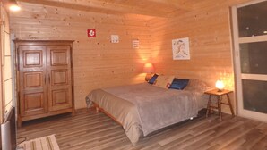 Quarto com painéis de madeira, uma cama, um guarda-roupa de madeira, um abajur e uma janela.