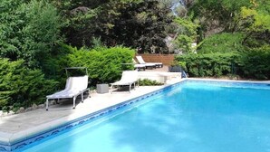 Piscina retangular com borda azulejada, cercada por vegetação exuberante e um deck de madeira com espreguiçadeiras.