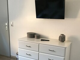 Uma cômoda branca com três gavetas e uma televisão de tela plana fixada na parede acima.