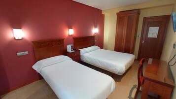 Quarto de hotel com duas camas de solteiro, mesa de cabeceira de madeira, escrivaninha e guarda-roupa.